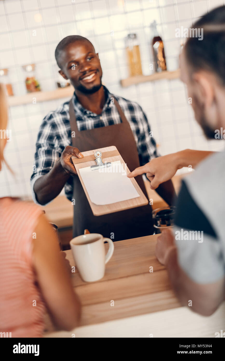 handsome smiling african american barista giving menu to clients on bar ...