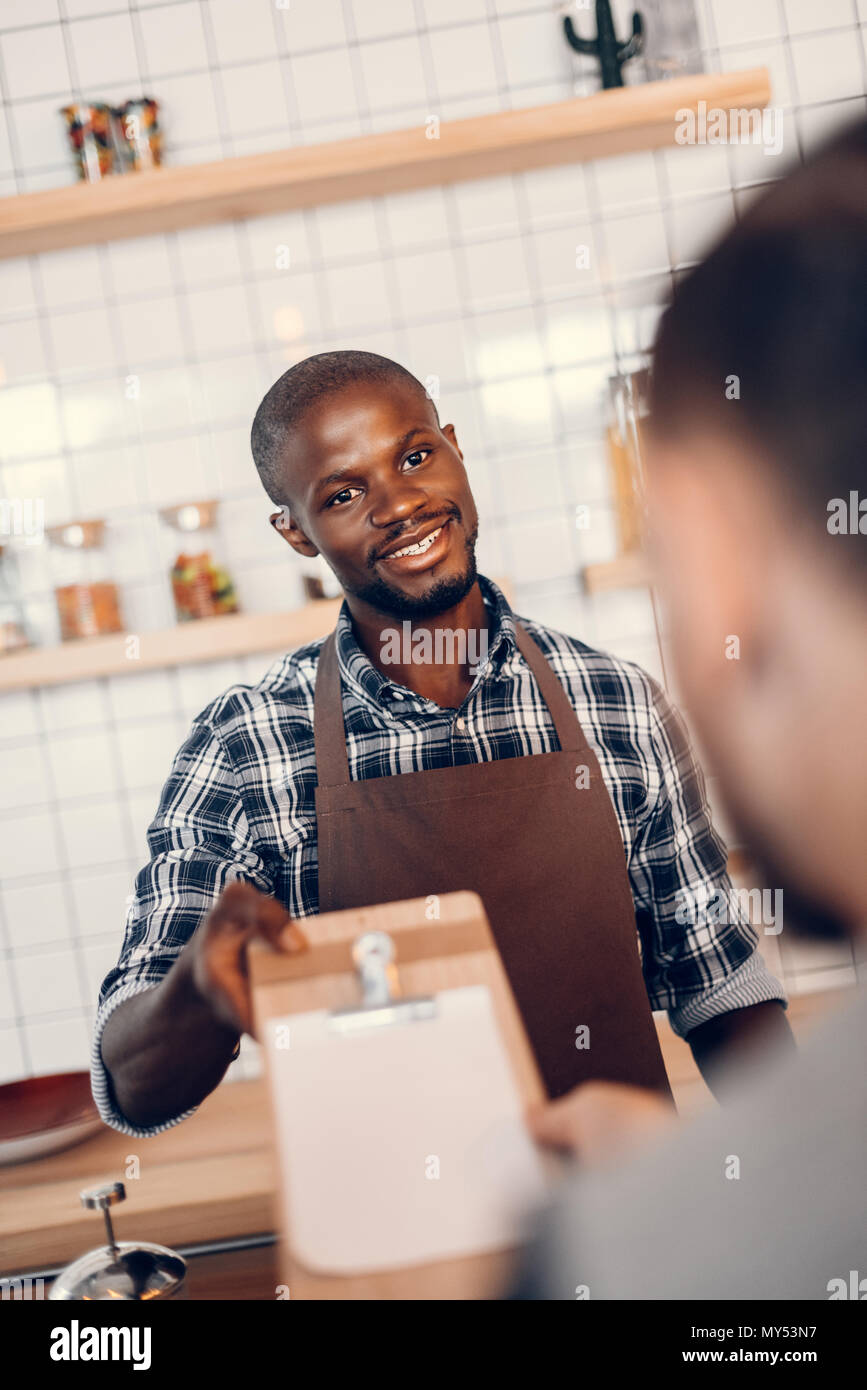 handsome cheerful african american barista giving menu to client on bar ...