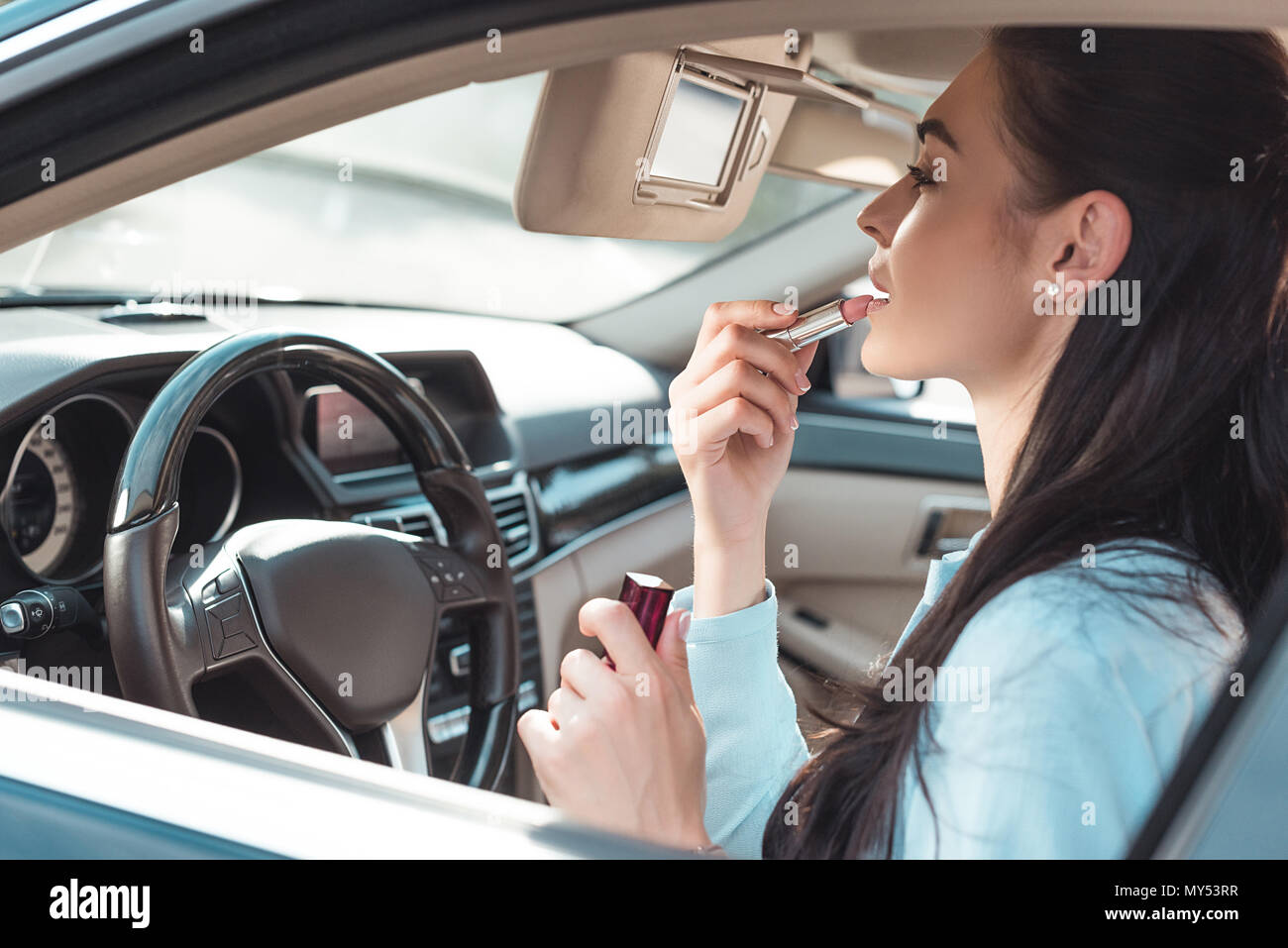 Young attractive woman applying lipstick in car, using a sun visor ...