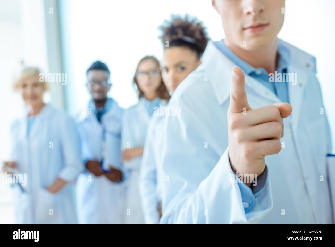 Young doctor in lab coat pointing his finger with group of young ...