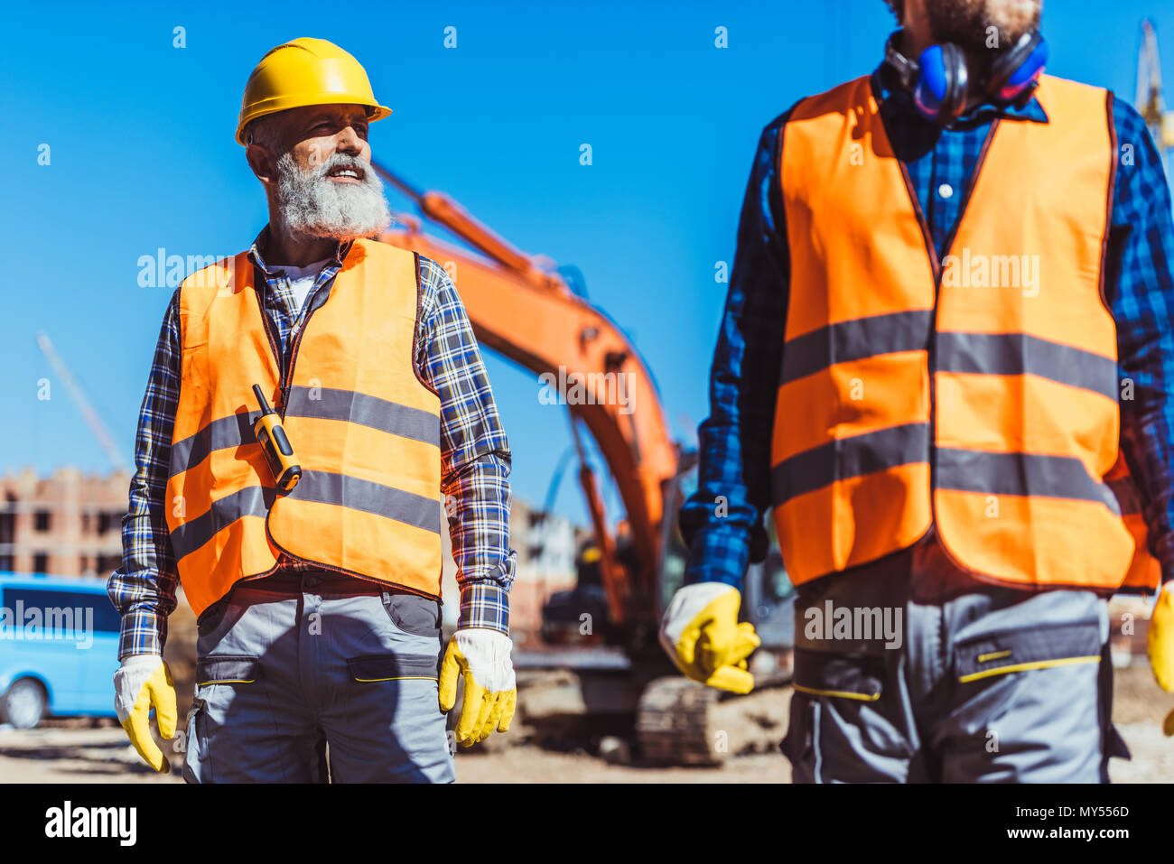 Two workers in reflective vests and hardhats standing at construction ...
