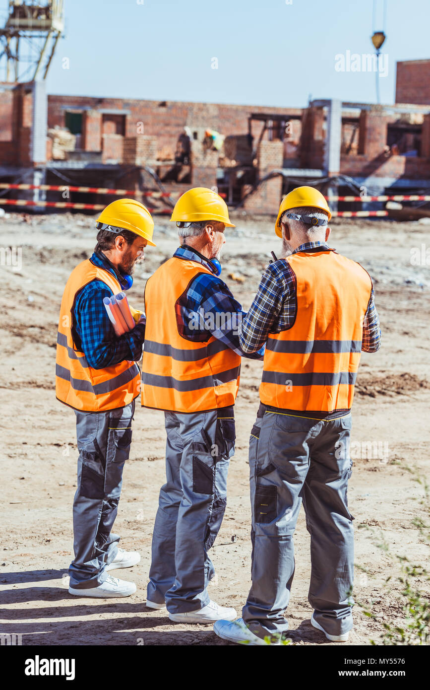 Three workers in hardhats and reflective vests standing at construction ...