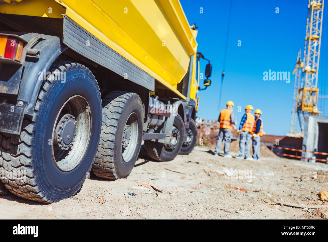 Three builders in uniform standing near a big yellow tip truck at ...