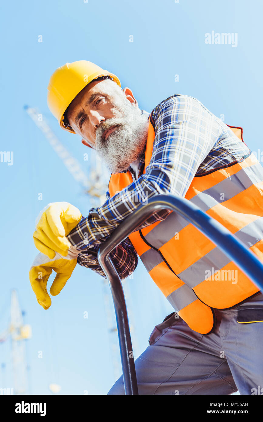 Bearded construction worker in reflective vest and hardhat leaning on ...