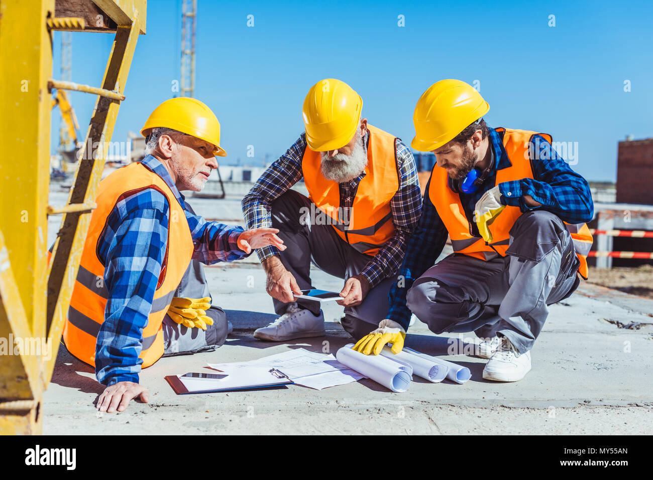 Three construction workers sitting on concrete at construction site ...