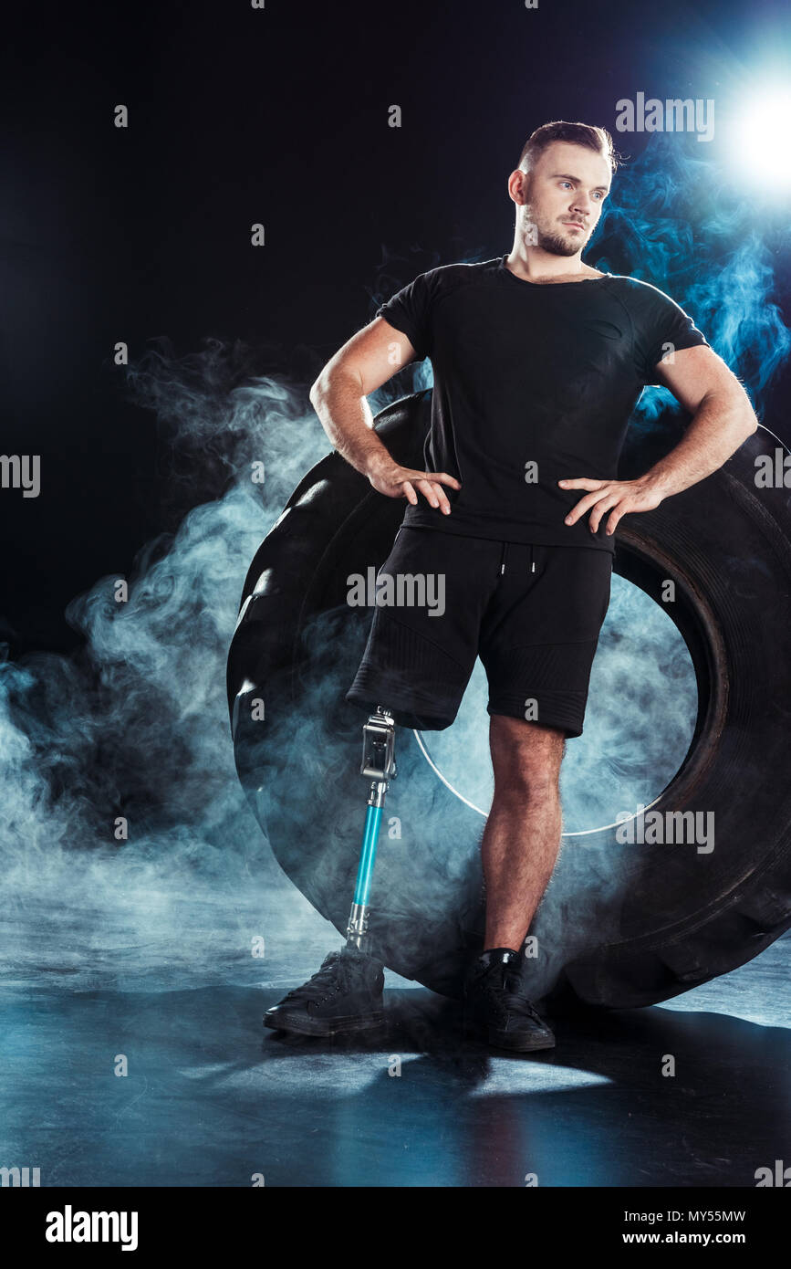 young sportsman with leg prosthesis standing akimbo while leaning on ...