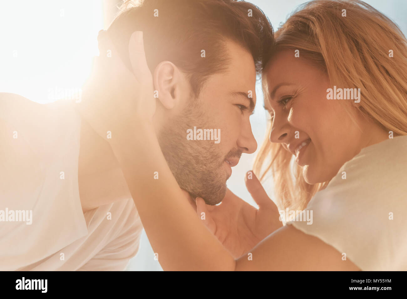 close-up portrait of beautiful cuddling couple in front of sun flare ...