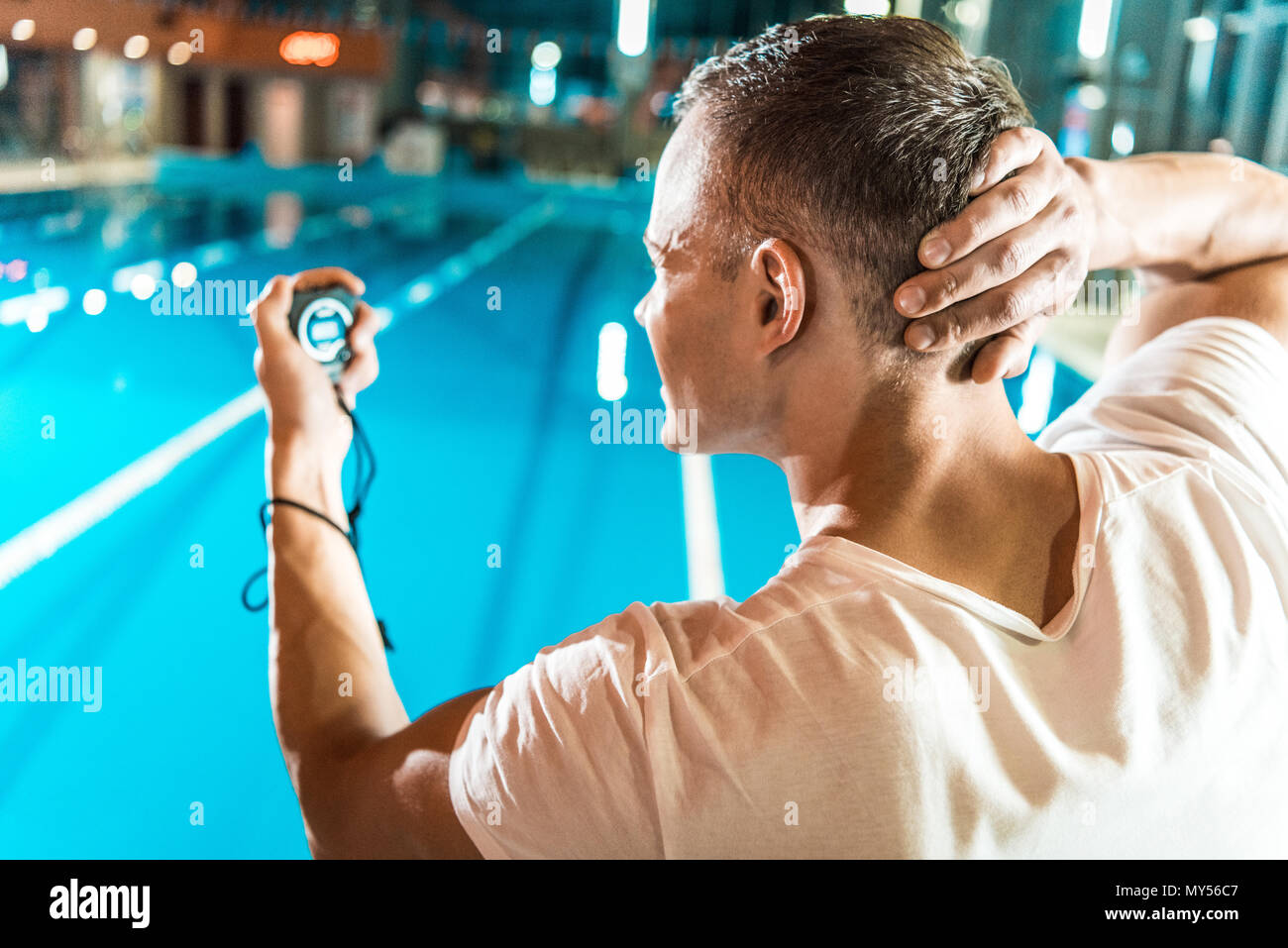 handsome swim trainer with timer standing at competition swimming pool ...
