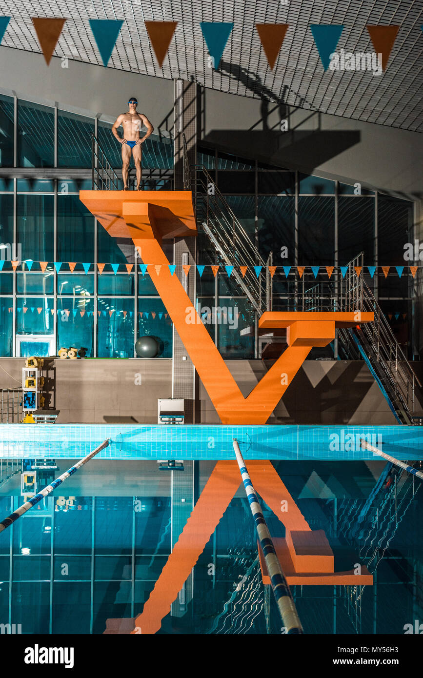 swimmer standing on diving platform ready to jump at swimming pool ...