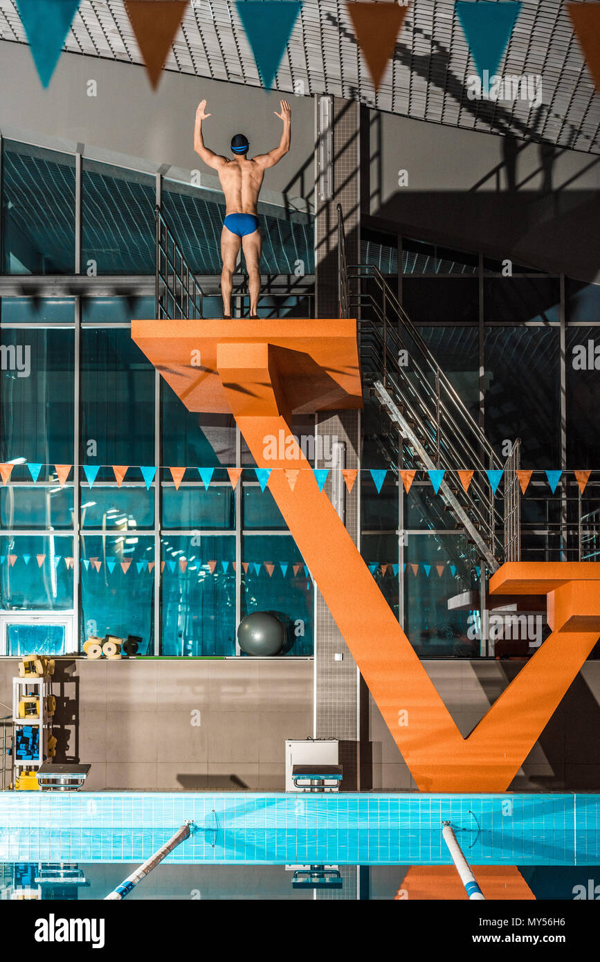 swimmer standing on diving platform ready to jump at swimming pool ...