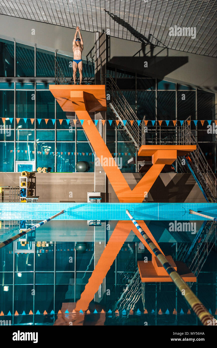 swimmer standing on diving platform ready to jump at swimming pool ...