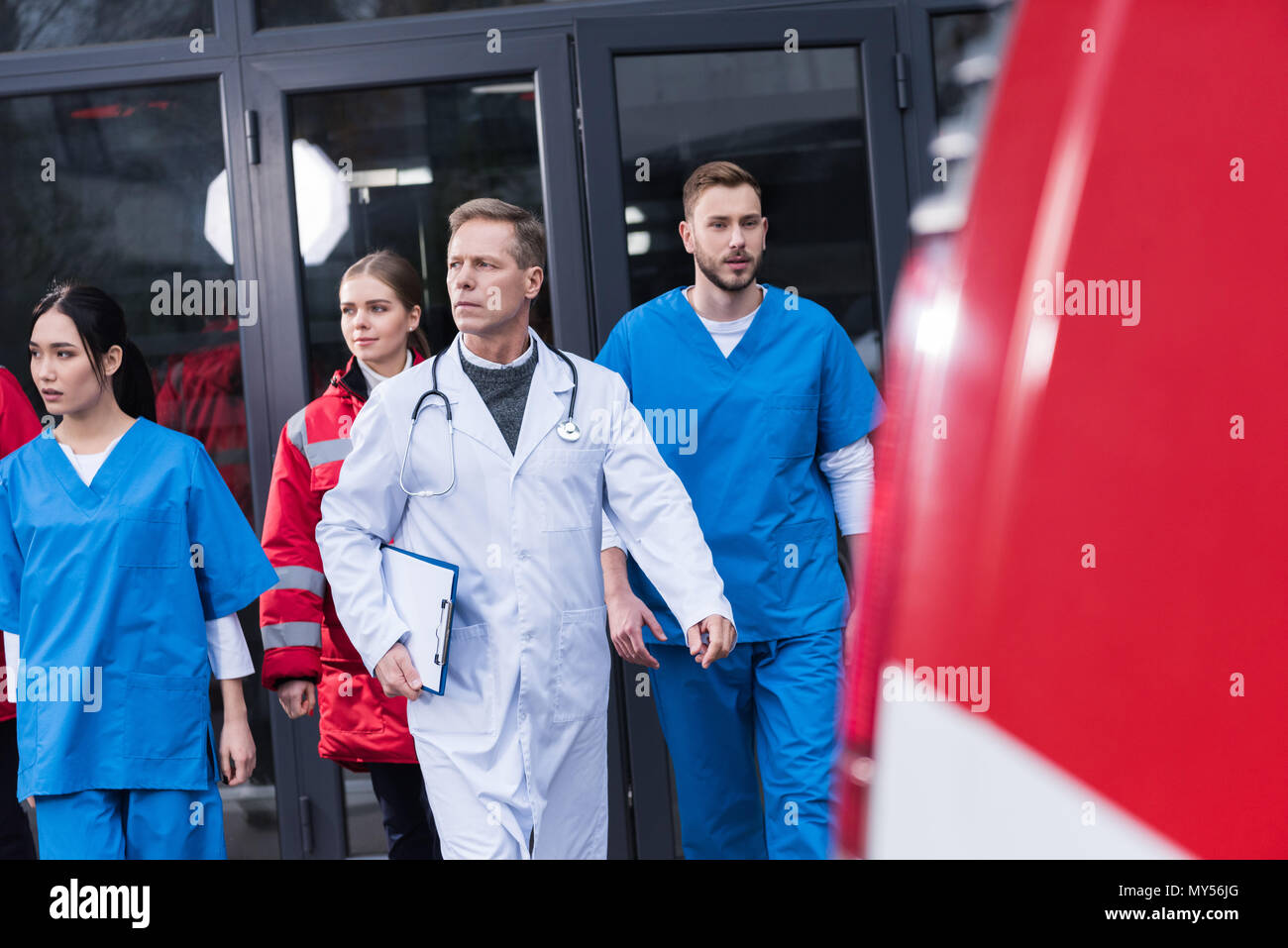 team of serious paramedics with doctor going from hospital to ambulance ...