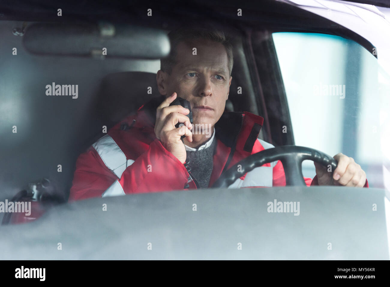 serious paramedic sitting in ambulance on driver seat and talking by ...