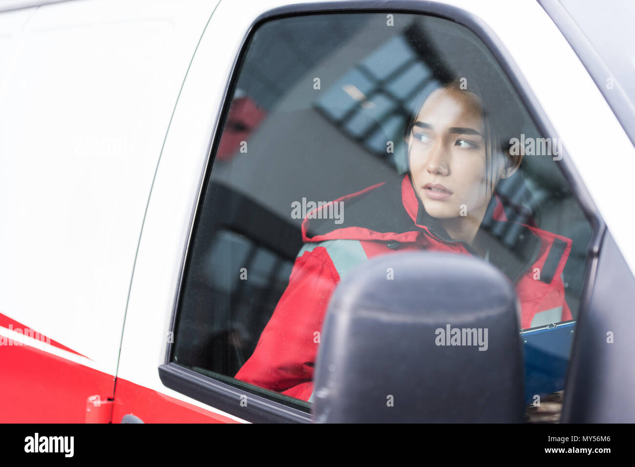 young Asian female paramedic sitting in ambulance and looking away ...