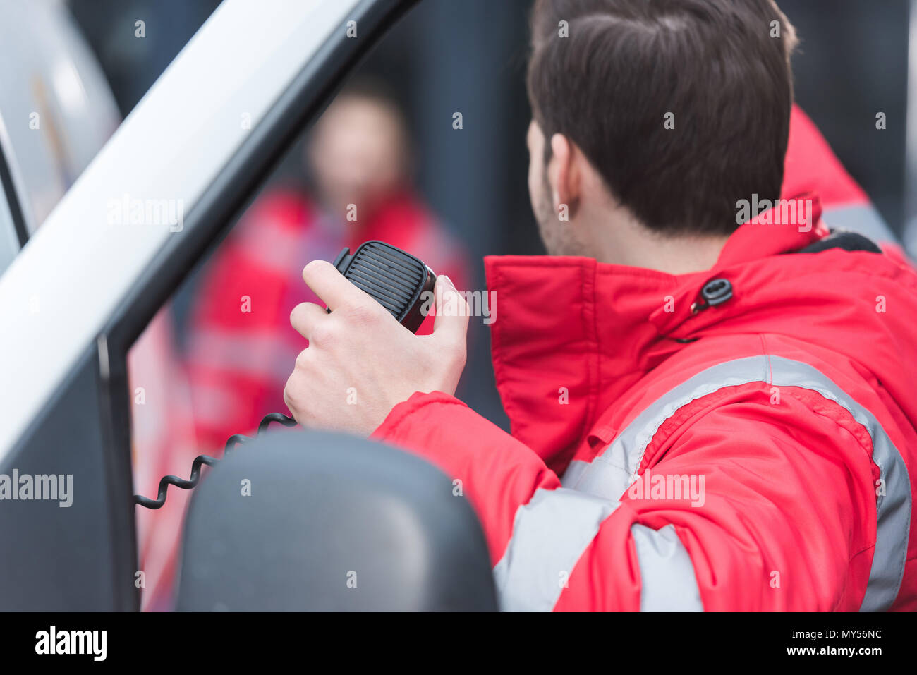 male paramedic talking by portable radio and showing something to ...