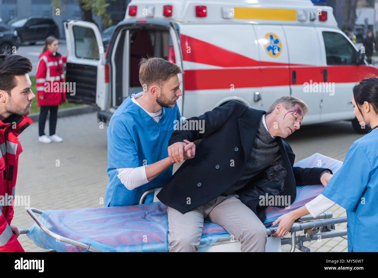 young paramedics helping injured man lie down on ambulance stretcher ...
