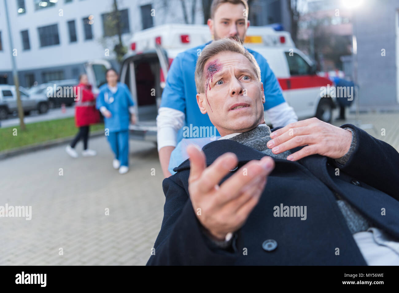 scared injured man with wound on head lying on ambulance stretcher ...