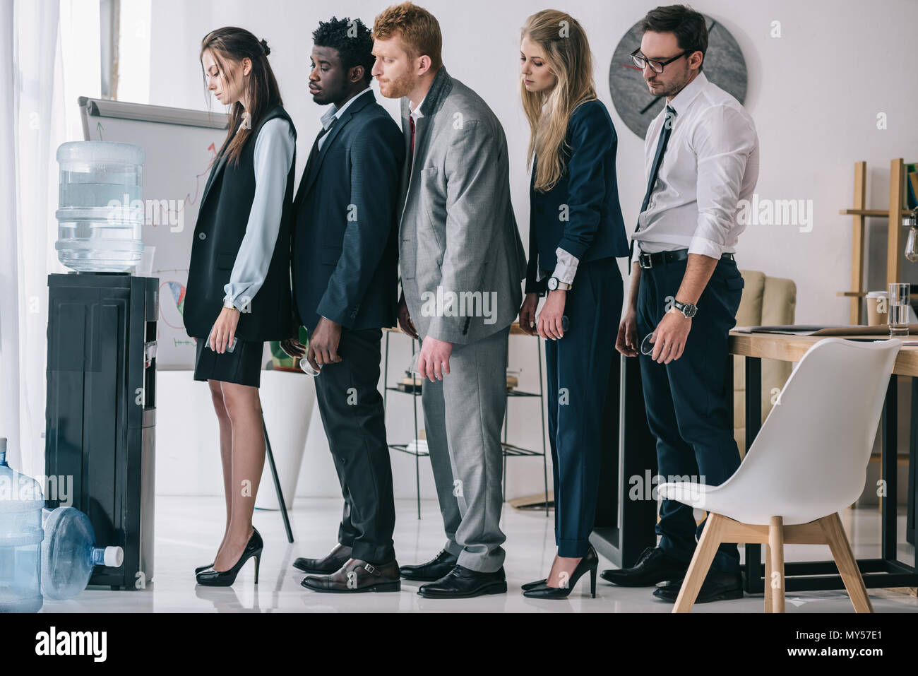 side view of business colleagues standing in queue for water dispenser ...