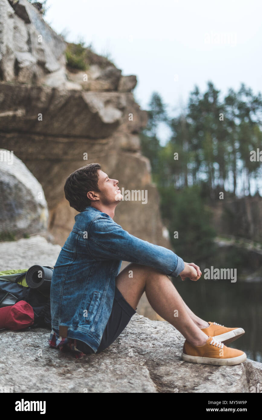 thoughtful young man relaxing on cliff near lake Stock Photo - Alamy