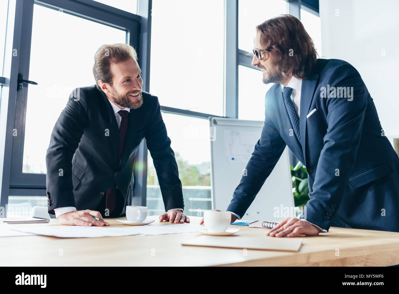 two businessmen in formal wear smiling each other while working together in office Stock Photo ...