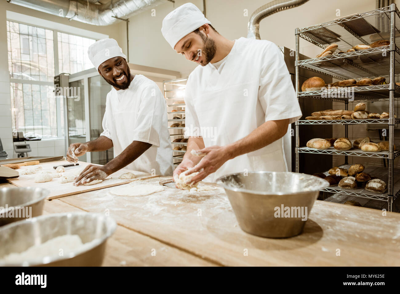 happy bakers kneading dough together at baking manufacture and talking ...