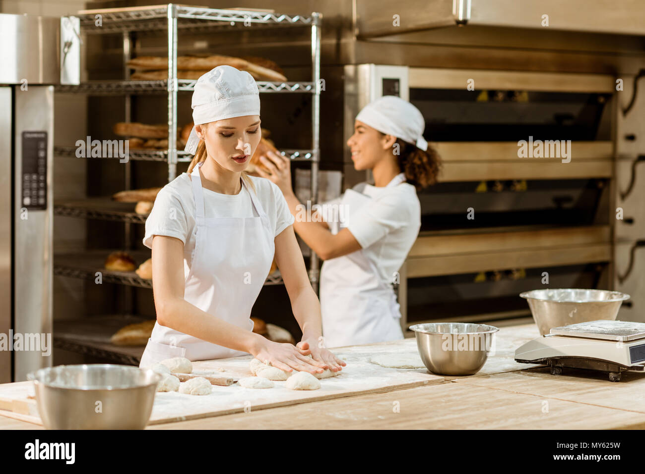young attractive female bakers working together at baking manufacture ...