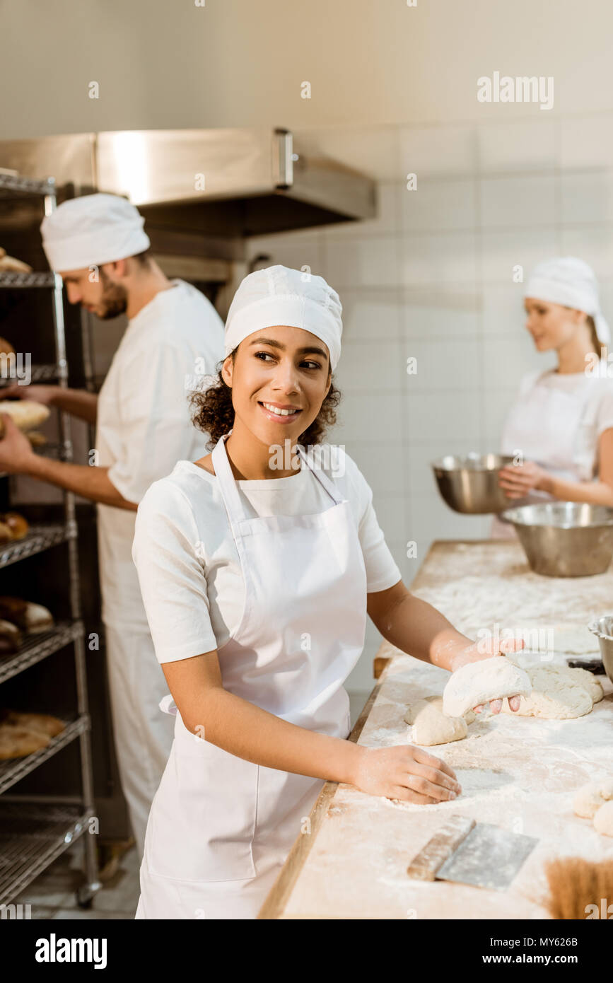 happy female baker kneading dough at baking manufacture while her ...