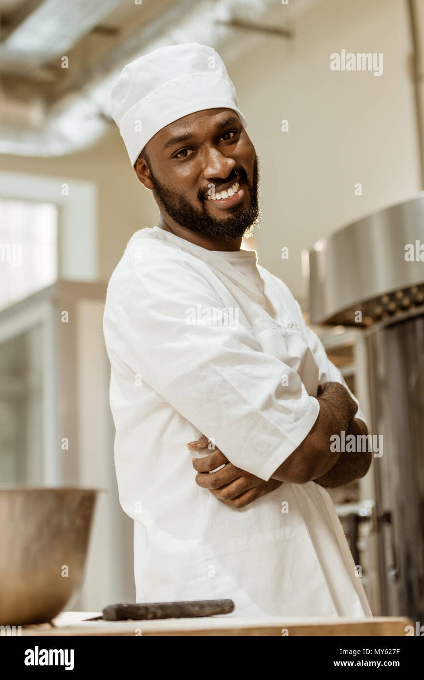 handsome african american baker with crossed hands looking at camera on ...