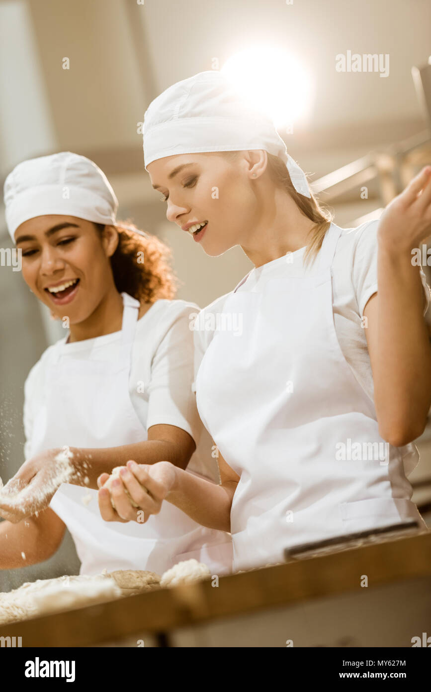attractive female bakers kneading dough together at baking manufacture ...