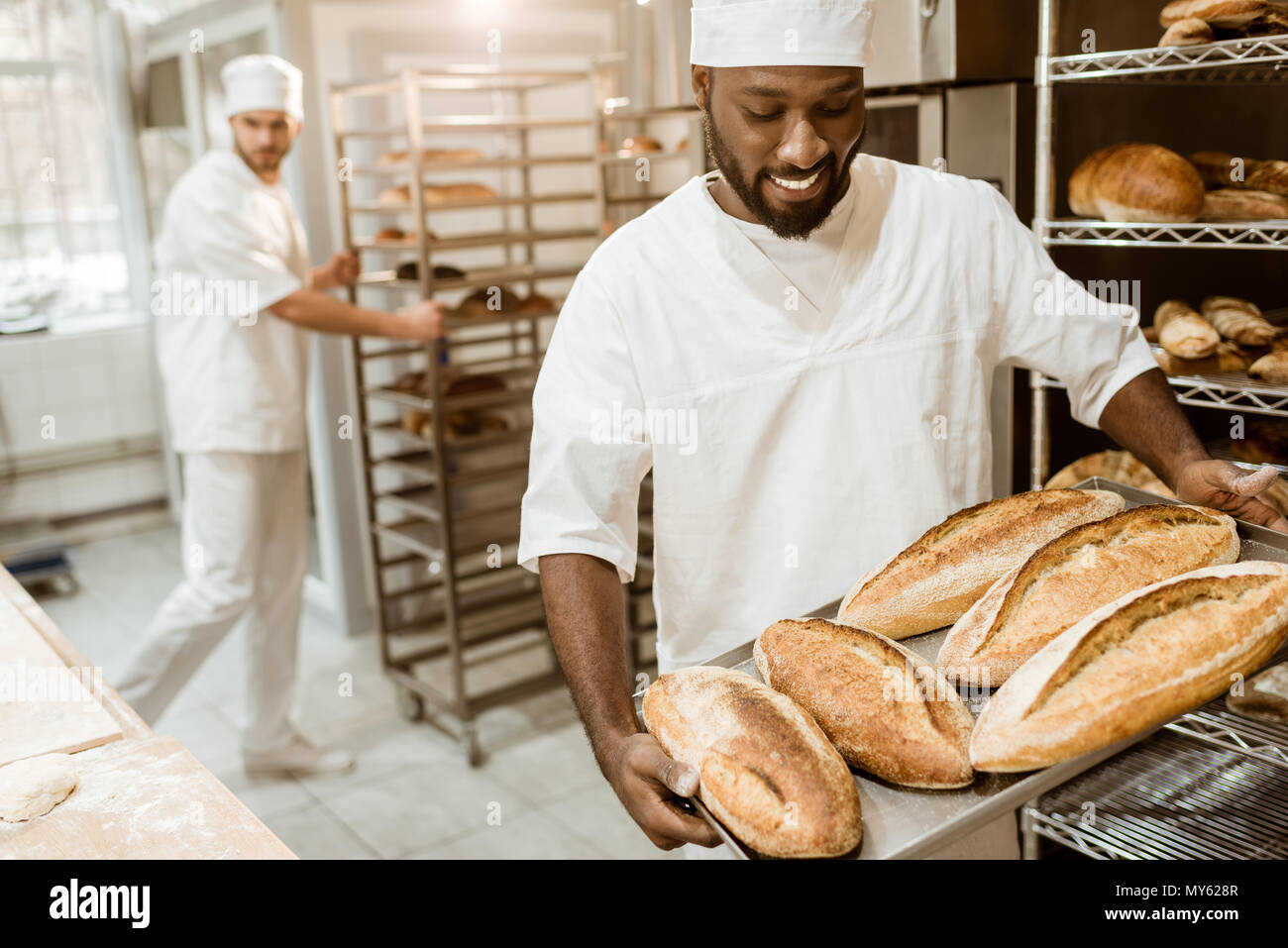 handsome african american baker taking bread loaves from oven at baking ...