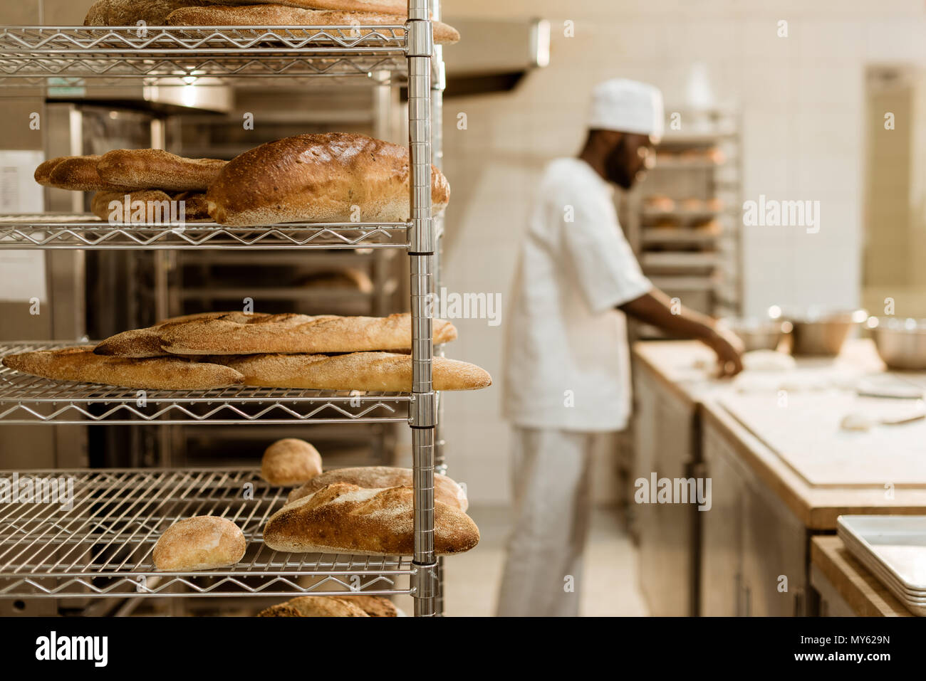 african american baker preparing raw dough at workplace with shelves of ...