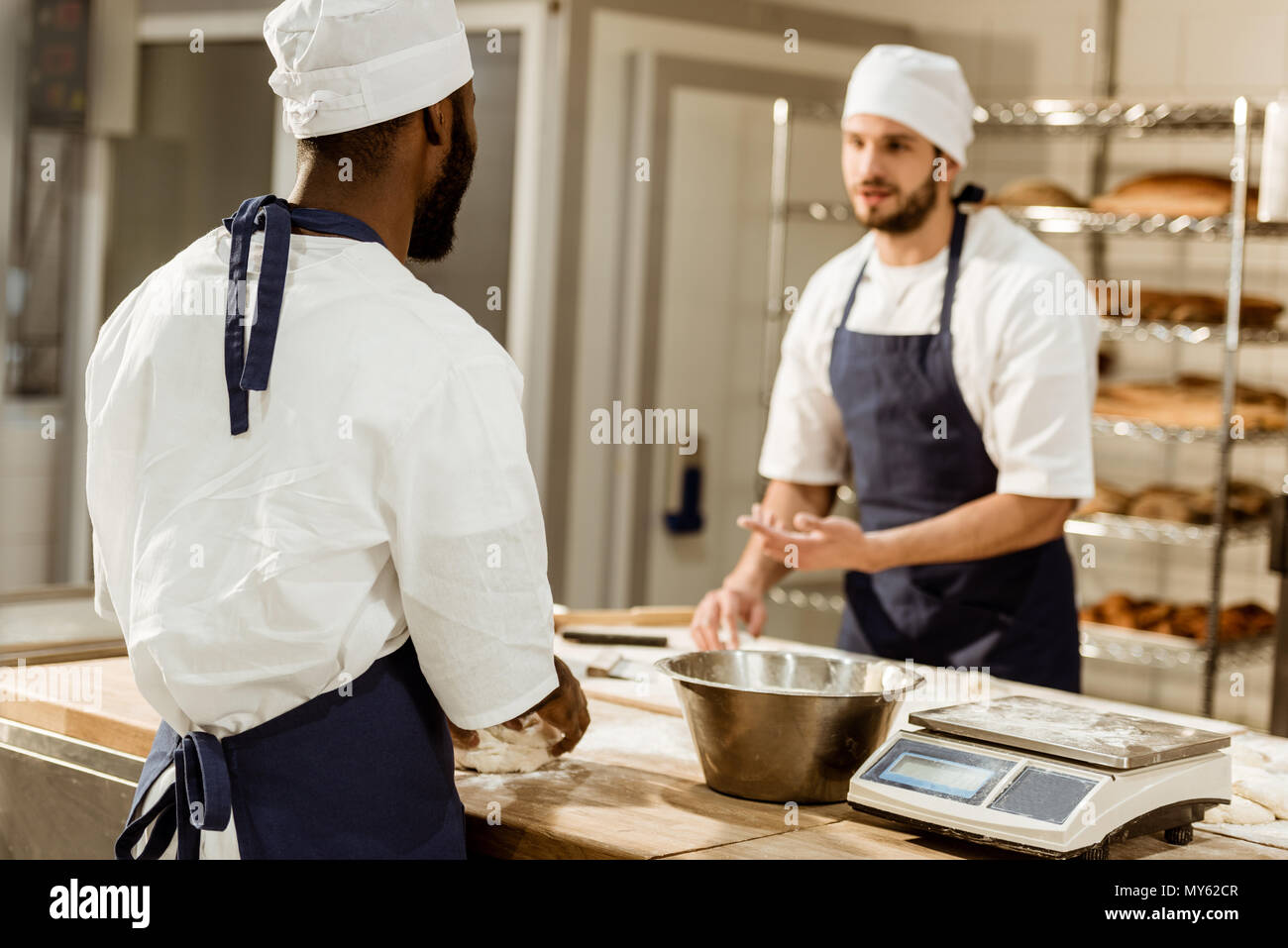 bakers in uniform kneading dough together at baking manufacture Stock ...