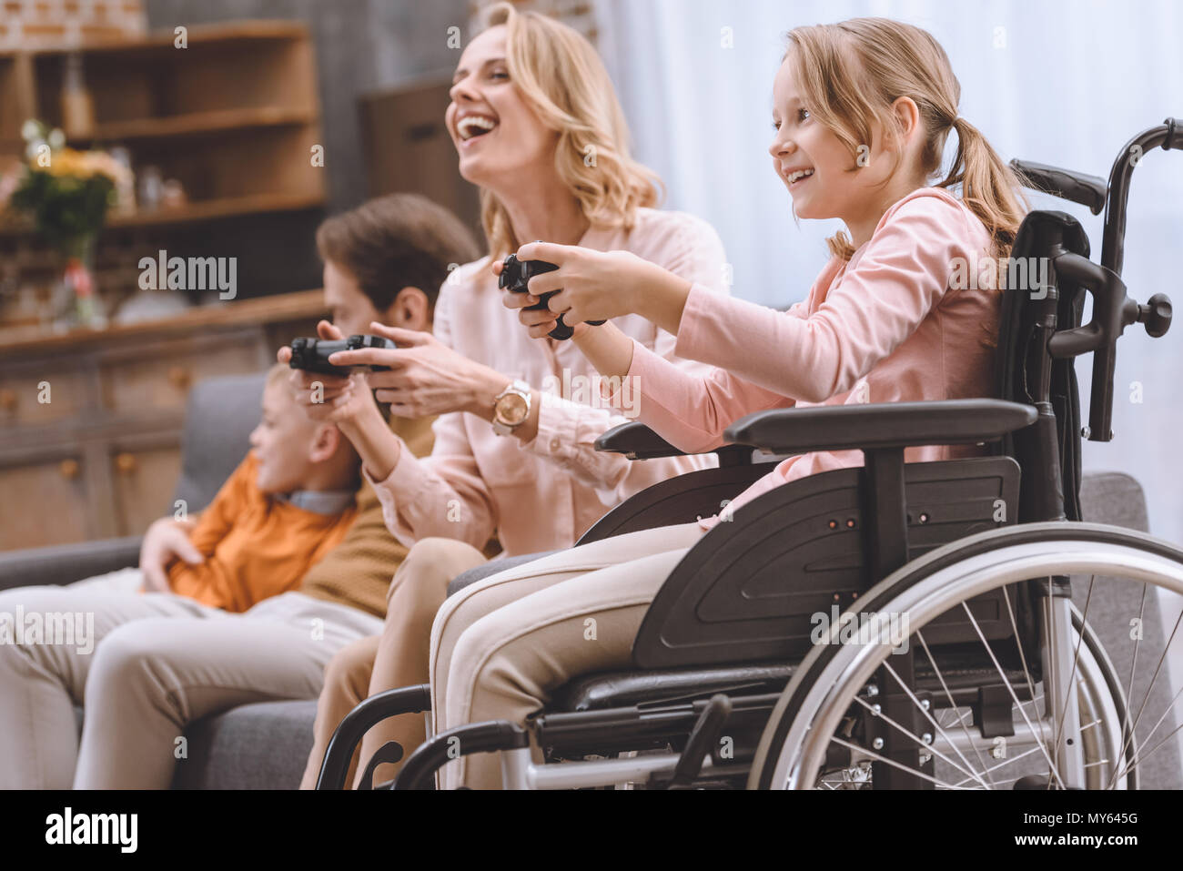 happy family with disabled child in wheelchair playing with joysticks ...