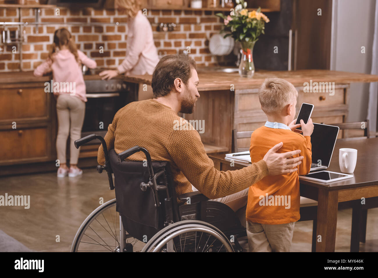 back view of disabled father in wheelchair and little son using ...