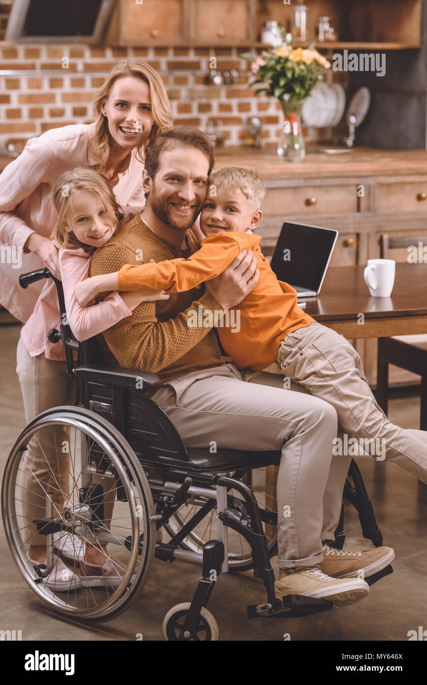 happy family with two kids and father in wheelchair hugging and smiling ...