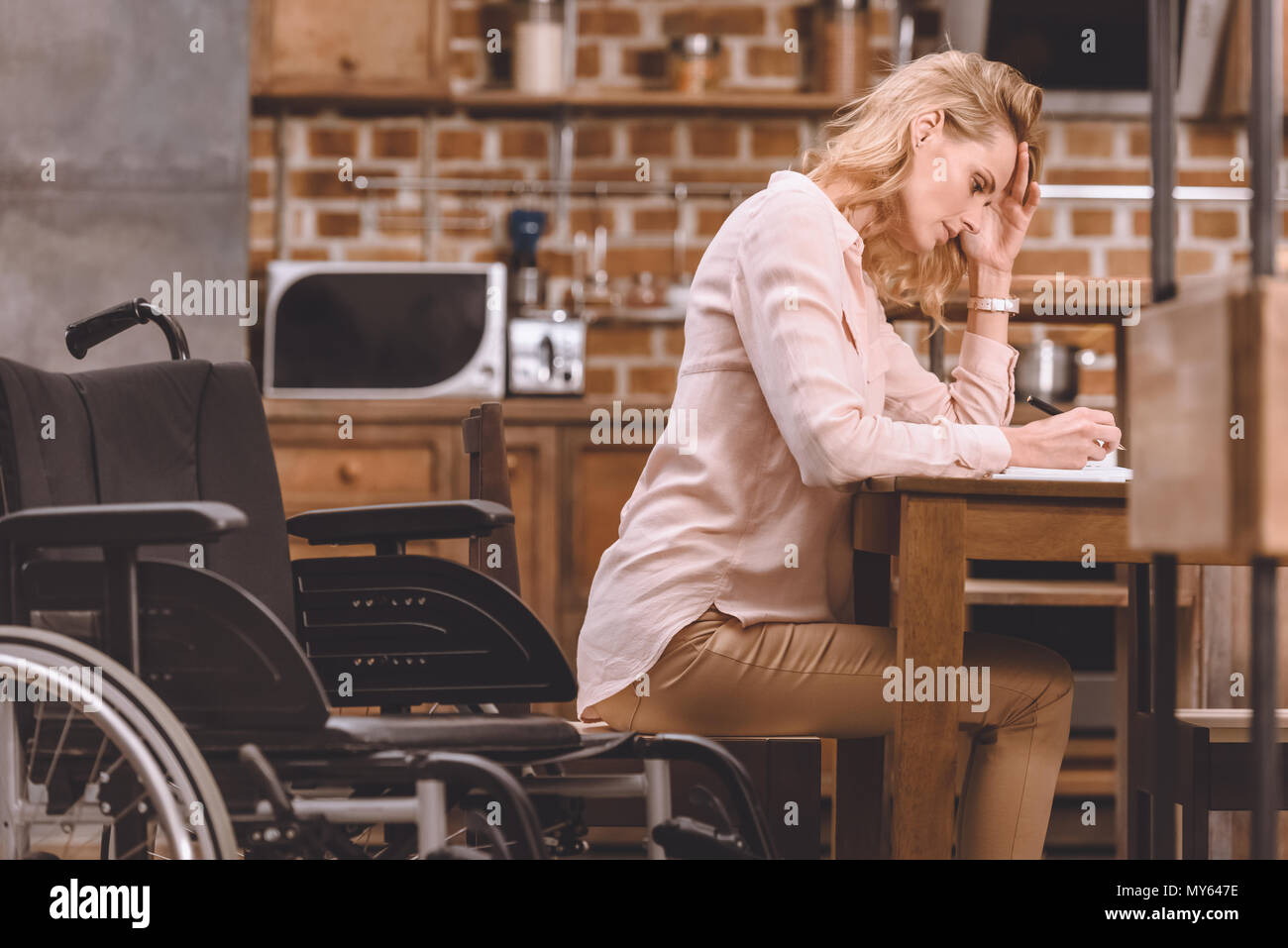 side view of disabled woman in wheelchair taking notes while working at ...