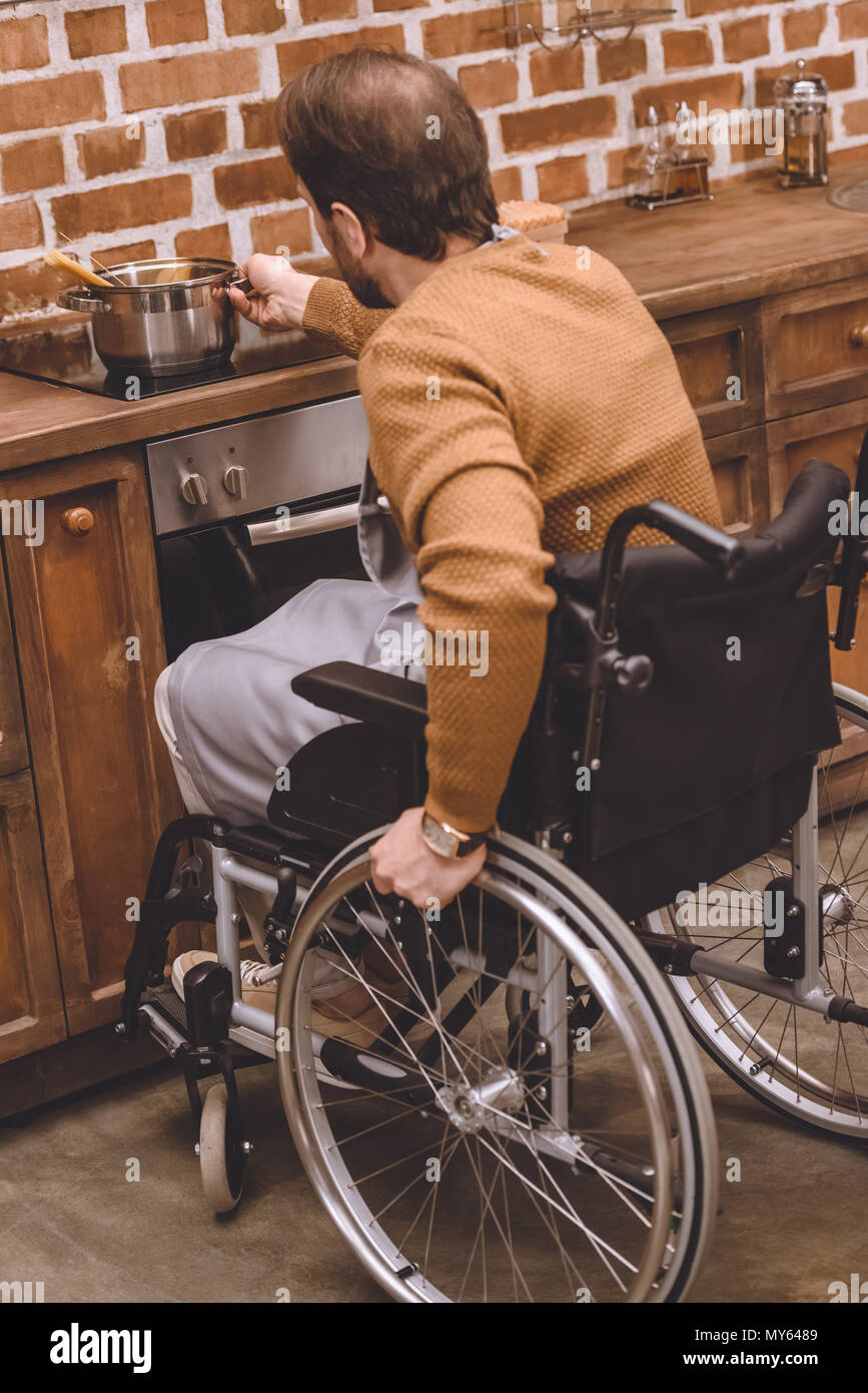 back view of disabled man in wheelchair holding pan while cooking at ...