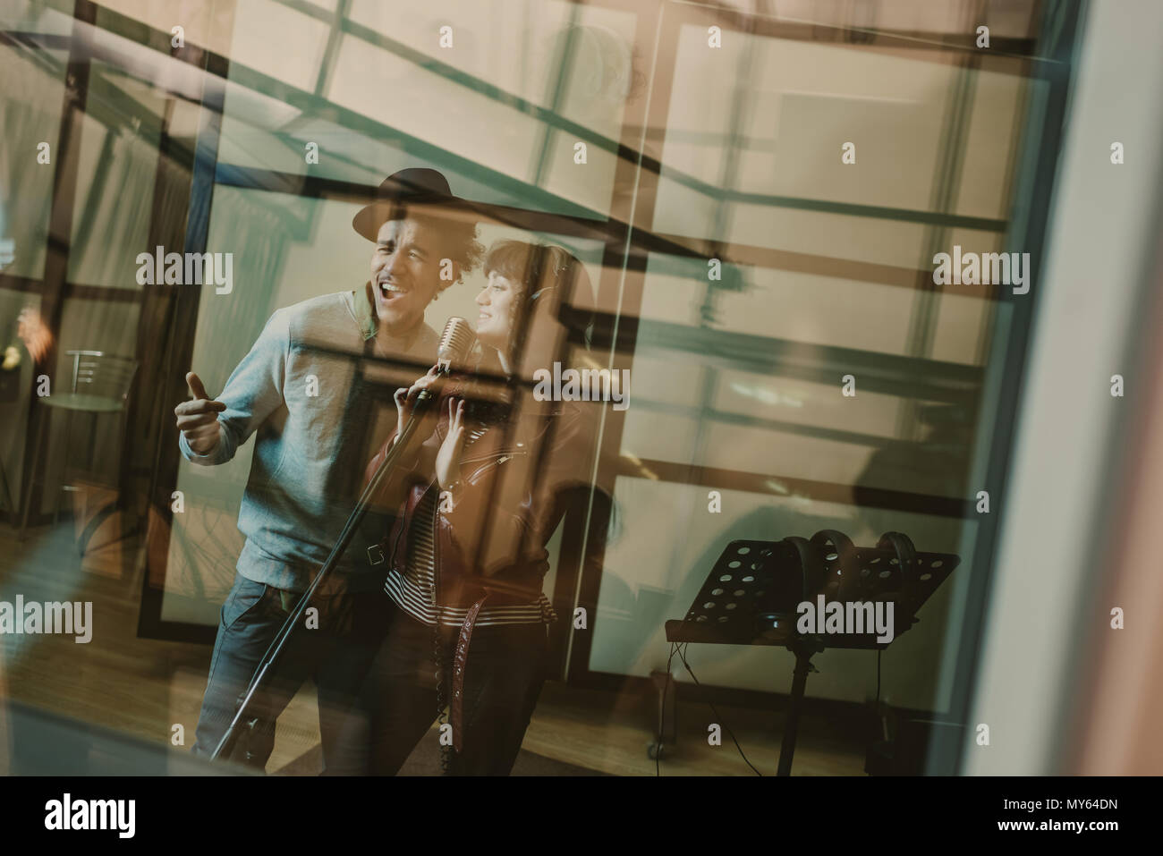 young talented singers couple recording song behind glass at studio ...