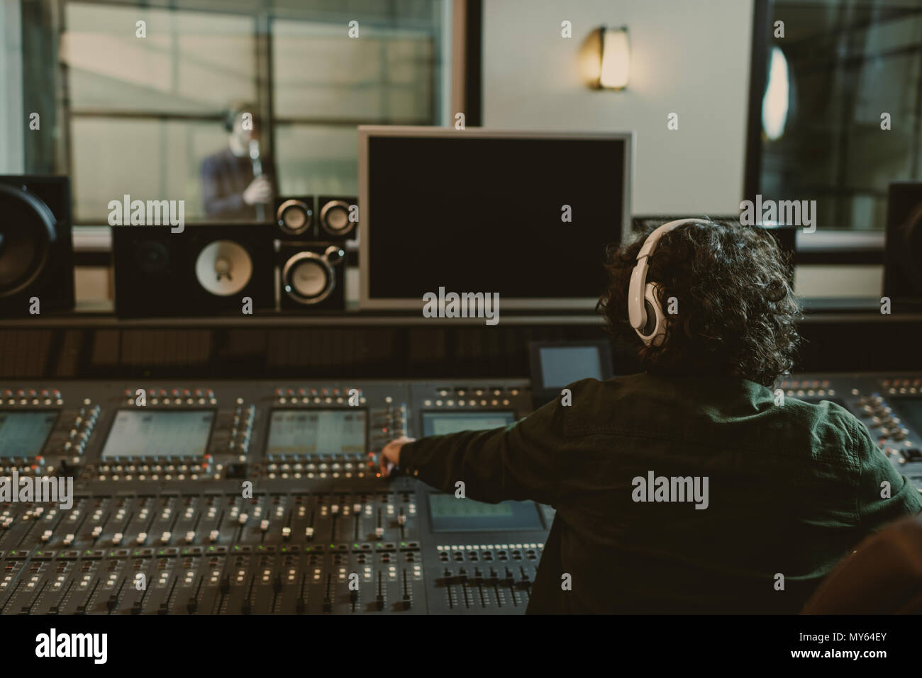 back view of sound producer working at studio while recording song ...