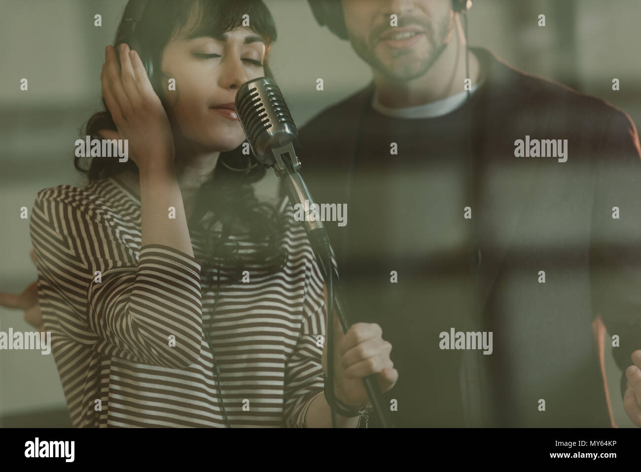young singers performing song behind glass in recording studio Stock ...