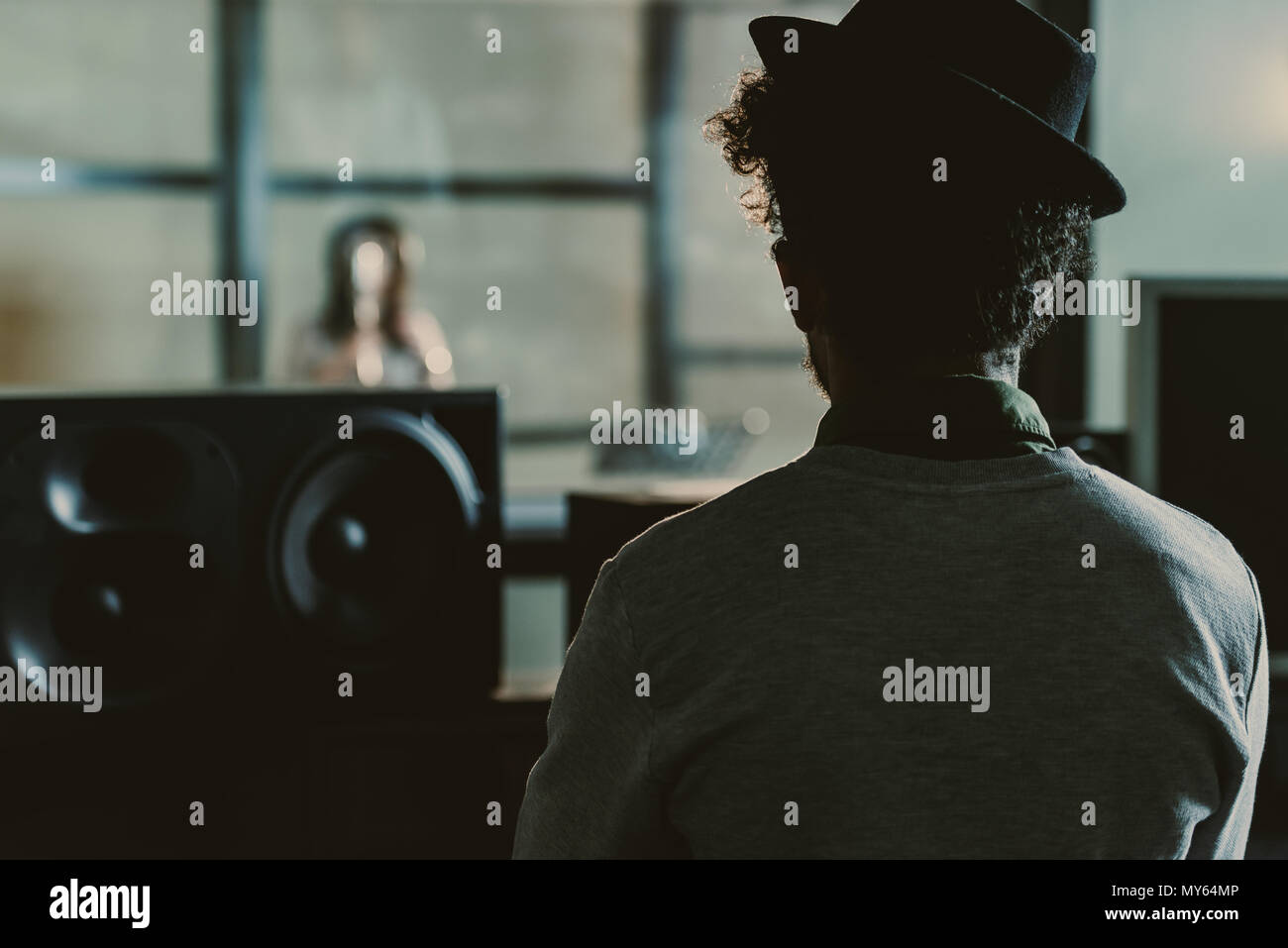 rear view of sound producer looking at singer recording song behind ...