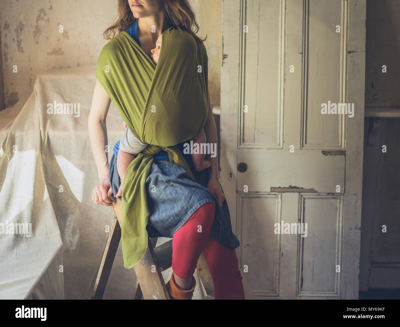 A young mother is sitting on a ladder with her baby in a room being ...