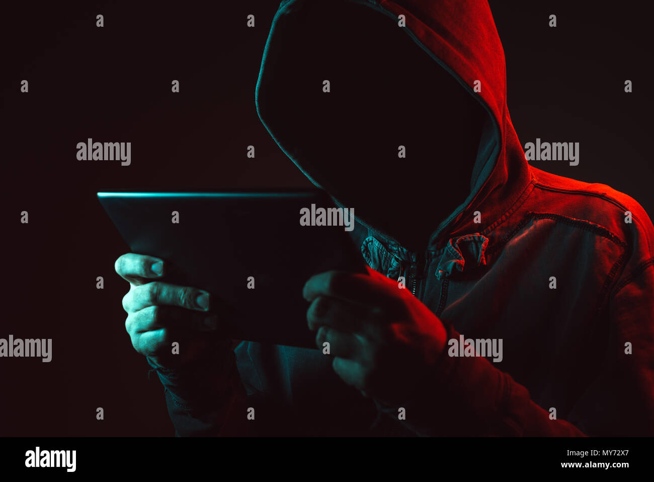 Faceless man with hoodie holding tablet computer in dark room, blue and ...