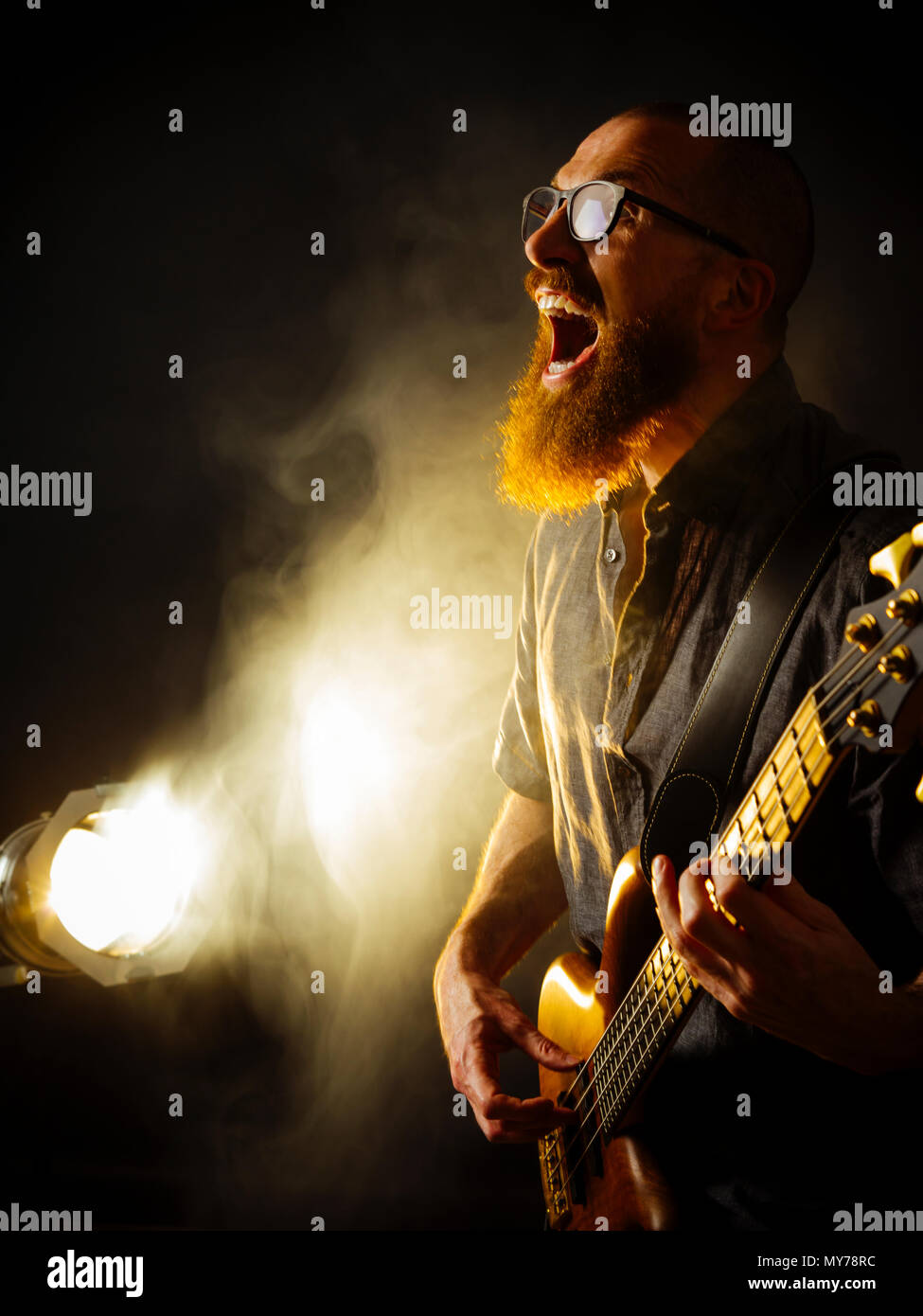 Photo of a screaming bass player with a beard playing in a dark club ...