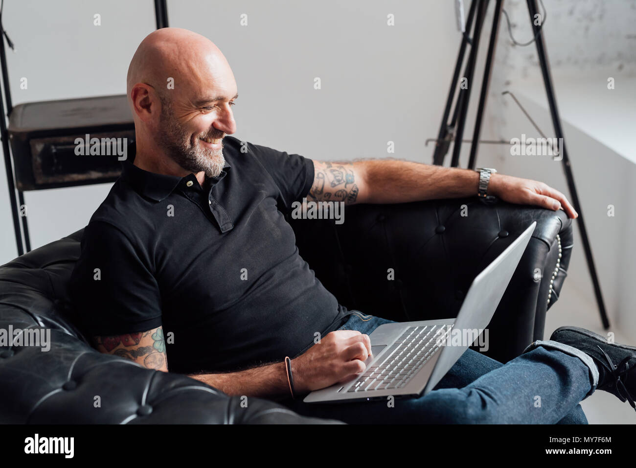 Man in armchair using laptop smiling Stock Photo - Alamy