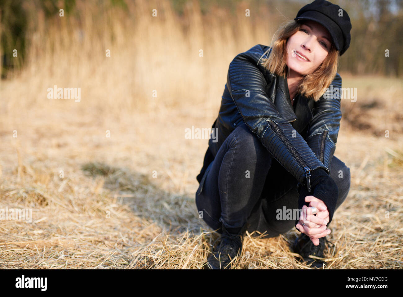 Cool woman wearing cap crouching on field straw, portrait Stock Photo ...