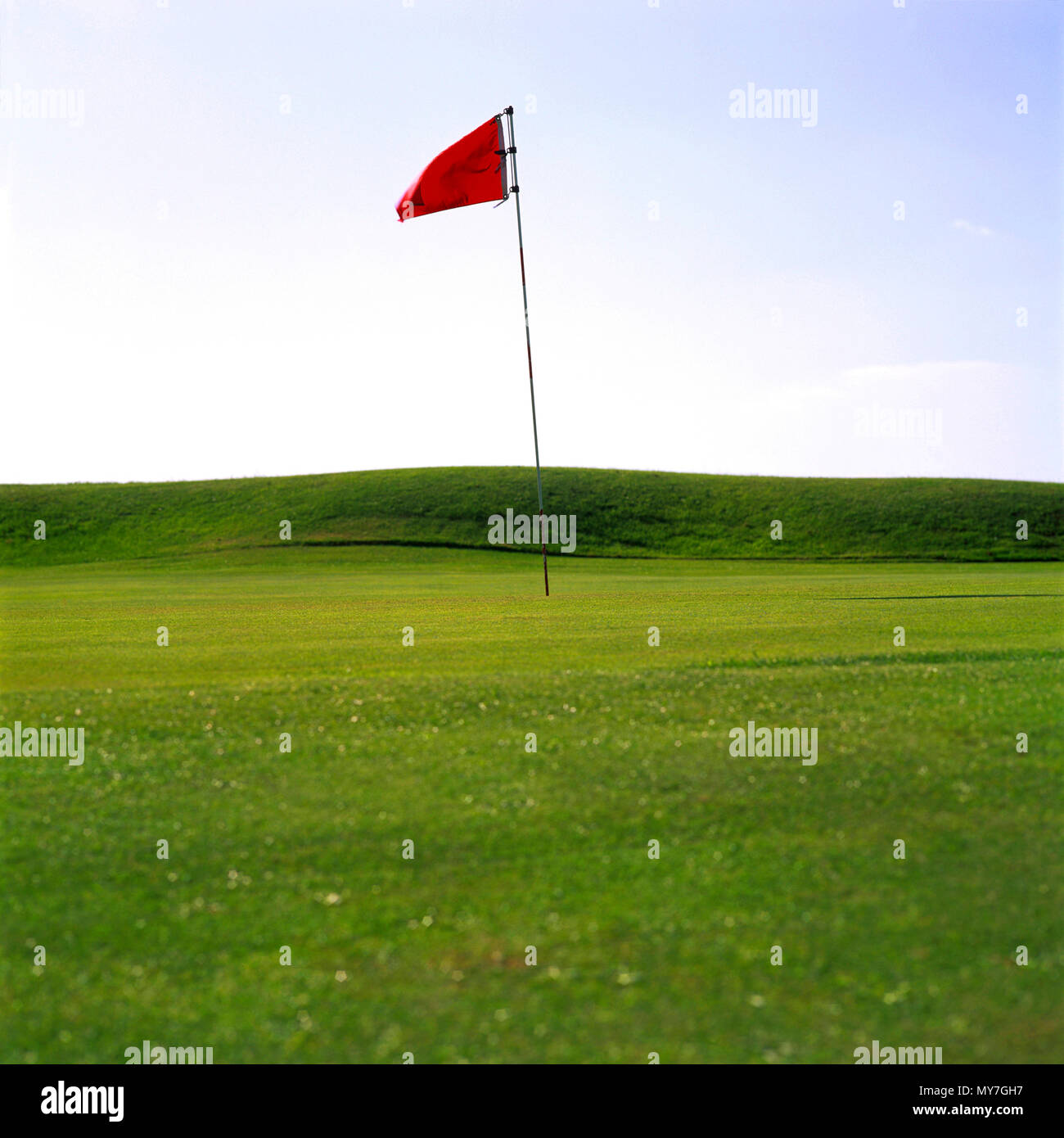 Bright green golf course with red flag marking the hole under clear ...