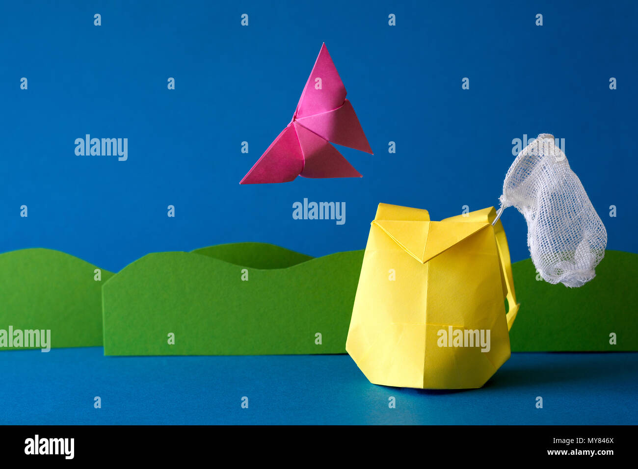 Paper backpack with butterfly net on grass field at blue background ...