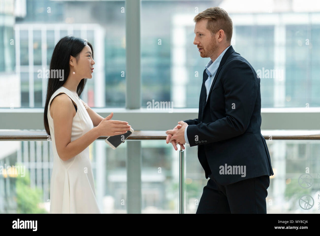 Businessman and businesswoman standing beside window, in conversation ...