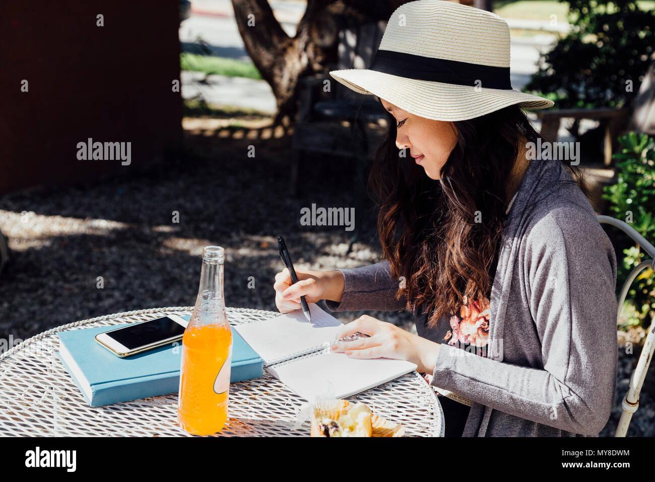 Young woman sitting outdoors, writing in notebook Stock Photo - Alamy